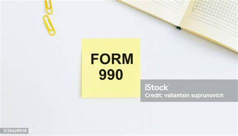 사무실 클립과 플래너가있는 흰색 배경에 격리 된 노란색 스티커 메모에 990 텍스트 비문을 작성하십시오 세금 마감일 및 세금 문서 개념 Internal Revenue
