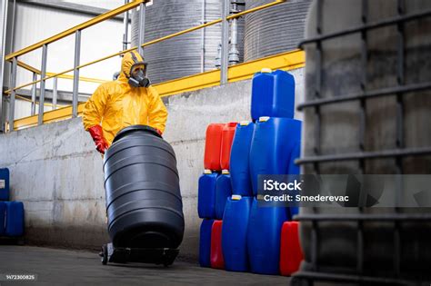 현대 화학 공장에서 위험한 화학 물질을 옮기는 동안 보호 복과 가스 마스크를 착용 한 근로자 백그라운드에서 산성이있는 대형 탱크 저장소 위험물에 대한 스톡 사진 및 기타