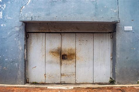 푸른 벽 배경에 녹 얼룩과 벗겨진 페인트가 있는 낡고 풍화된 차고 문으로 도시의 쇠퇴와 빈티지의 매력을 보여줍니다 강철에 대한 스톡 사진 및 기타 이미지 Istock