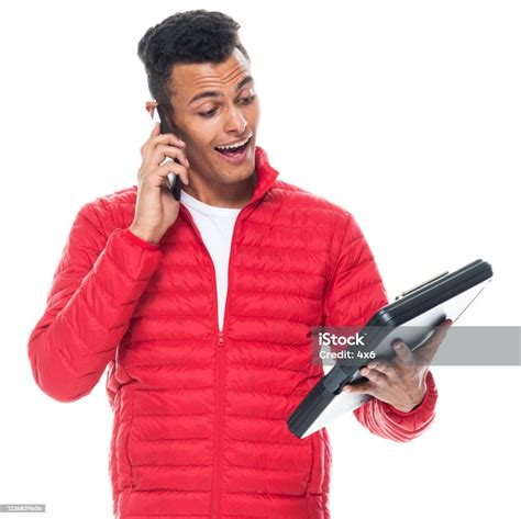티셔츠를 입고 목록을 들고 스마트 폰을 사용하여 흰색 배경 앞에 서있는 아프리카 인종 남성 20 24세에 대한 스톡 사진 및
