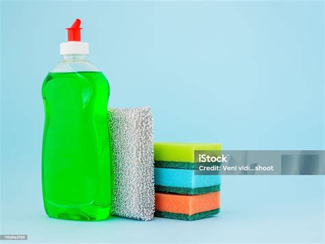 녹색 식기 세척액이있는 투명 한 병과 파란색 배경에 다른 색상의 4 개의 거품 스폰지 공간을 복사합니다 부엌 세제 가정용 화학
