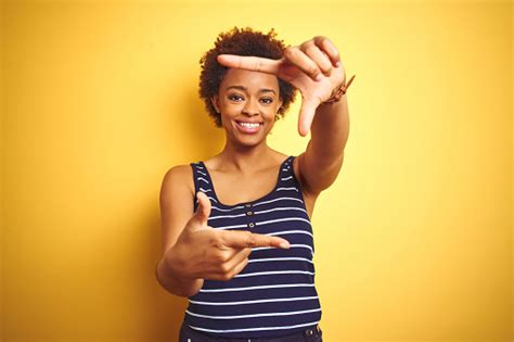 아름다운 아프리카 계 미국인 여성은 행복한 얼굴로 손과 손가락으로 프레임을 만드는 고립 된 노란색 배경 위에 여름 티셔츠를 입고 있습니다 창의력과 사진 개념 T 셔츠에 대한