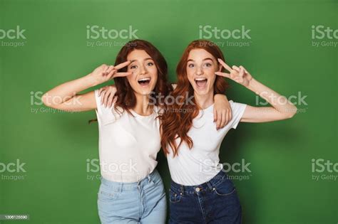 녹색 배경에 고립 된 얼굴에 미소와 승리 표지판을 보여주는 두 빨간 머리 십대 여성의 초상화 20 29세에 대한 스톡 사진 및
