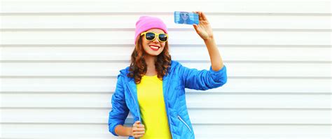 화려한 핑크색 모자를 쓰고 스마트폰으로 셀카를 찍는 현대의 행복한 미소 짓는 젊은 여성의 초상화 흰색 배경에 파란색 재킷 20 29세에 대한 스톡 사진 및 기타 이미지