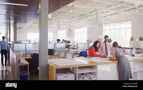 Wide Angle Shot Of Male And Female Architects Meeting In Busy Multi Cultural Open Plan Office