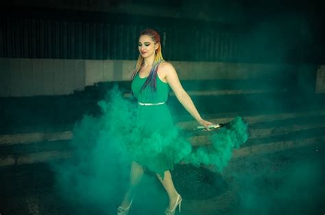 아프리카 머리띠와 따뜻한 봄 도시의 거리에서 밝은 녹색 연기와 함께 포즈를 취하는 화려한 메이크업과 녹색 드레스를 입은 귀여운 소녀 땋은 머리에 대한 스톡 사진 및 기타