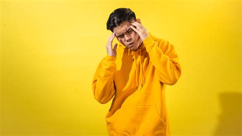 노란색 후드티를 입은 젊은 아시아 남자가 고통에 양손과 눈을 감고 머리를 만지며 노란색 배경에 서 있습니다 두통 스트레스 또는 좌절감을 위한 스튜디오 컨셉 35 39세에