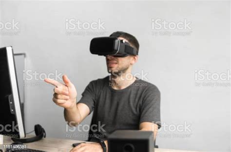 젊은 남자 착용 가상 현실 고글 헤드셋과 컴퓨터에 대 한 사무실에 앉아 연결 기술 새로운 세대 남자는 손으로 물건을 만지거나 Vr을 제어 하려고 합니다 가상현실에 대한 스톡
