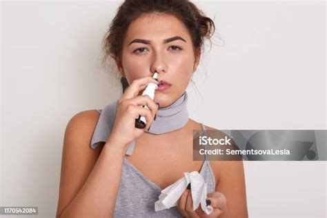 콧물이 많은 젊은 건강에 해로운 여성의 실내 촬영 손에 손수건 들고 감기에 걸린 여인 독감이나 계절 알레르기로 고통받고 스프레이를 사용하여 흰색 회색 스튜디오 배경에 고립