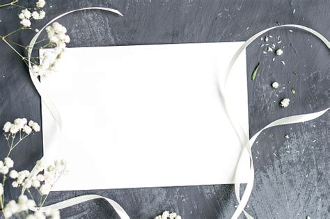 작은 흰색 꽃 구성과 미니멀 한 스타일의 새틴 리본에 빈 종이 모형 회색 복사 공간 배경에 레터링 텍스트 인사말 카드 결혼식 초대장을위한 흰색 시트 결혼 의식에 대한 스톡