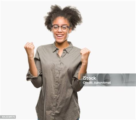 축 하 하는 고립 된 배경 위에 안경을 쓰고 젊은 아프리카 미국 여자 놀라게 하 고 무기와 성공을 위한 제기 및 오픈 눈 깜짝 놀라게 우승자 개념입니다 긍정적인 감정 표현에