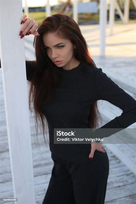 저녁에 녹색 양복을 입은 빨간 머리를 가진 아름다운 젊은 유행 소녀는 여름에 바다 바다의 물가에 하얀 부두에 서 있습니다 25 29세에 대한 스톡 사진 및 기타 이미지