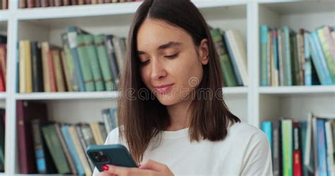 Student Girl Standing In Library And Using Smartphone Texting Message