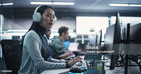 기술 사무실 환경에서 컴퓨터로 작업하는 사려 깊은 젊은 엔지니어의 초상화 헤드폰을 끼고 블록체인 프로젝트를 위한 소프트웨어 코드를 작성하는 아름다운 아시아 여성 여성에 대한
