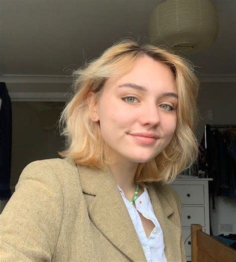 A Woman With Blonde Hair Wearing A Tan Blazer And White Shirt Smiling
