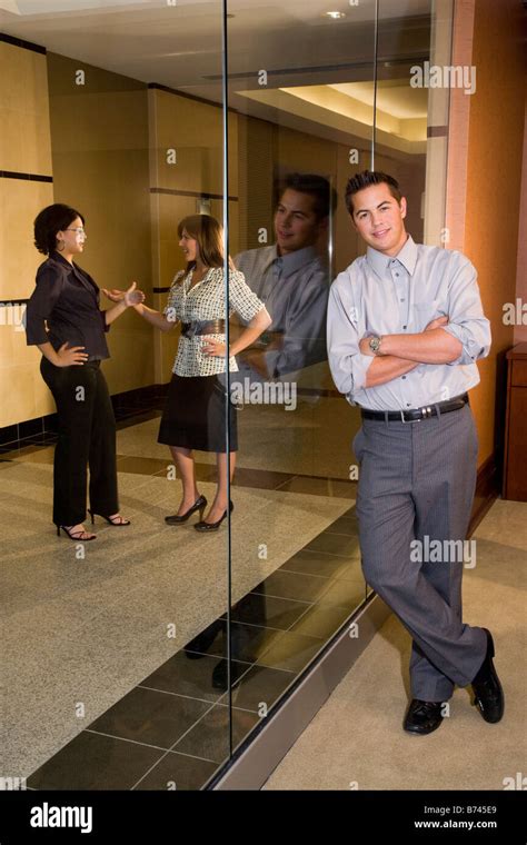 Office Worker Leaning On Glass Wall With Co Workers Chatting Outside