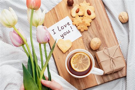 발렌타인 데이를 맞아 침대에서 즐거운 아침 식사 마음의 형태로 자신의 손으로 차와 쿠키 사랑하는 소녀에게 종이 선물 꽃에 대한 메모 가정의 방에 대한 스톡 사진 및 기타