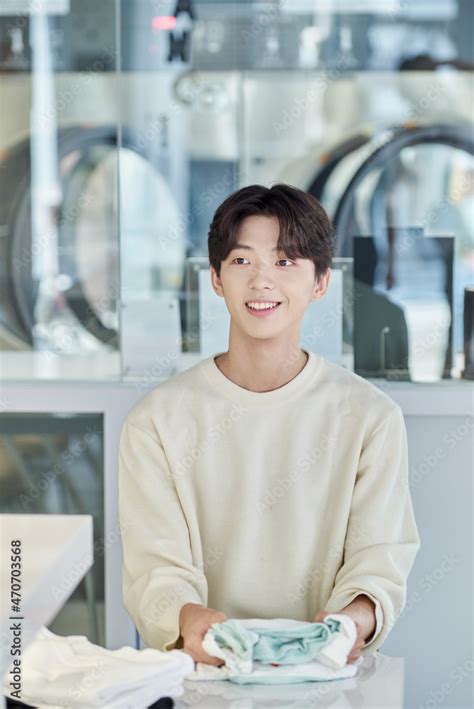 세탁기와 건조기 배경으로 깨끗한 옷감을 정리하고 있는 젊은 아시아 한국남자 남자 모델 Stock 写真 Adobe Stock