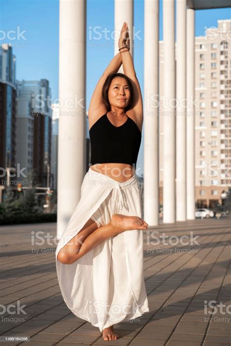 젊은 아시아 여성이 낮 동안 도시의 전망과 함께 야외에서 요가를 연습하고 있다 소녀는 푸른 하늘을 보며 아사나를 수행합니다 도시