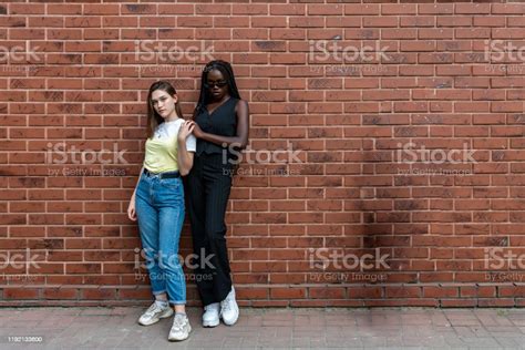 파란색 청바지와 노란색 티셔츠를 입은 젊은 유럽 소녀가 검은 색 줄무늬 옷과 빨간 벽돌 벽 위에 고립 된 선글라스를 입은