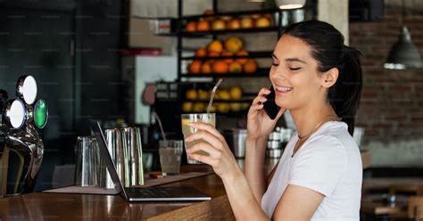 자유 시간 동안 커피숍에 혼자 앉아 있는 동안 휴대폰으로 전화를 걸고 있는 젊은 매력적인 여성 바에서 쉬는 동안 휴대폰으로