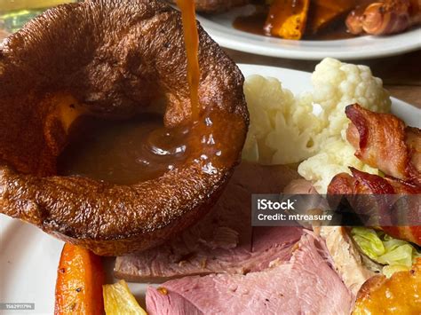 일요일 로스트 디너 식사 요크셔 푸딩 당근 파스닙 구운 감자 양배추 콜리플라워 담요에 담긴 돼지 구운 가몬 높은 전망이 포함된 흰색 접시에 쏟아지는 그레이비의 전체 프레임