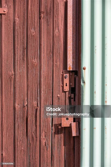 풍화 판자와 깨진 자물쇠가있는 오래된 문은 모두 밝은 녹색으로 칠해진 금속 벽 요소 옆에 빨간색 갈색으로 칠해졌습니다 0명에 대한 스톡 사진 및 기타 이미지 Istock