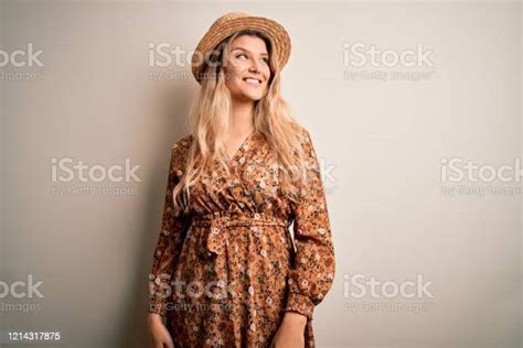 여름 드레스와 모자를 입고 고립 된 흰색 배경 위에 얼굴을 미소 자연스러운 표정으로 옆으로 바라보는 젊은 아름다운 금발 여성