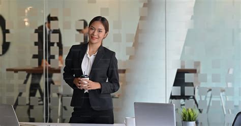 검은 정장을 입은 자신감 넘치는 여성이 사무실 회의실에서 테이크아웃 커피잔을 들고 동료들 위에 서 있다 사진 Unsplash의 양복 이미지