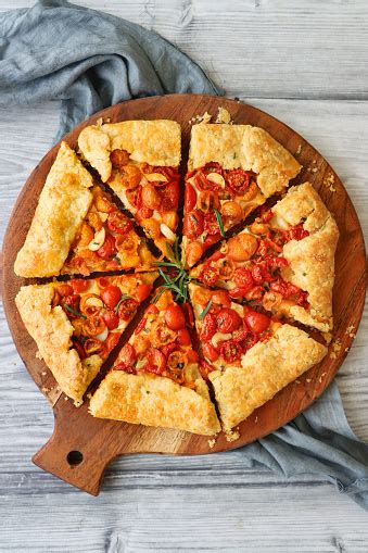 얇게 썬 갓 구운 수제 짭짤한 갈레트 레시피를 원형으로 회색 모슬린 페스토 체리 토마토 반쪽 부스러진 페타 치즈 브로마리 잎 퍼프 페이스트리 크러스트 회색 목간 배경 높은