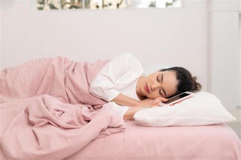 白い枕に横になりながらスマートフォンで寝ているアジアの若い女性の写真 プレミアム写真