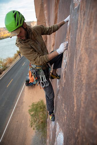 암벽 등반 장비를 착용한 모험심 많은 남자가 유타 주 모압의 길가 협곡의 바위면을 확장하면서 아래 길을 내려다보고 있다 가을에 대한 스톡 사진 및 기타 이미지 Istock