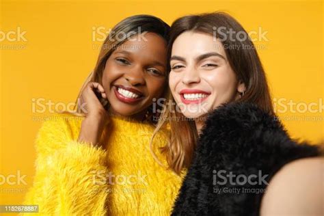 두 여자 친구 유럽과 아프리카계 미국인 검은 노란색 옷을 하 고 밝은 오렌지 벽 배경 스튜디오 초상화에 고립 된 포즈 Selfie 샷 하 고 사람들 라이프 스타일 개념입니다