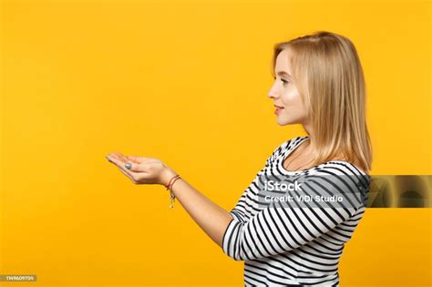 스튜디오에서 노란 주황색 벽 배경에 고립 된 손 손바닥에 뭔가를 들고 줄무늬 옷에 예쁜 젊은 여자의 측면 보기 사람들은 진심으로 감정 라이프 스타일 개념입니다 복사 공간을