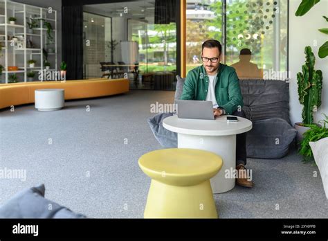 Male Computer Programmer With Glasses Working Over Laptop While Sitting On Sofa In Modern