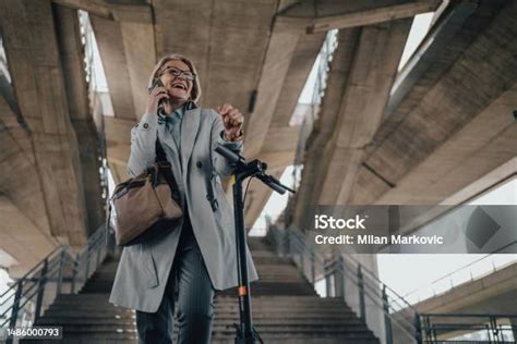 성숙한 비즈니스 우먼은 도시 교통을 더 쉽게 탐색하기 위해 전기 스쿠터로 출퇴근합니다 50 59세에 대한 스톡 사진 및 기타 이미지 50 59세 건강한 생활방식 건물