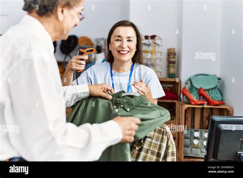 Middle Age Man And Woman Smiling Confident Scanning Clothes Using Bardcode Reader At Clothing