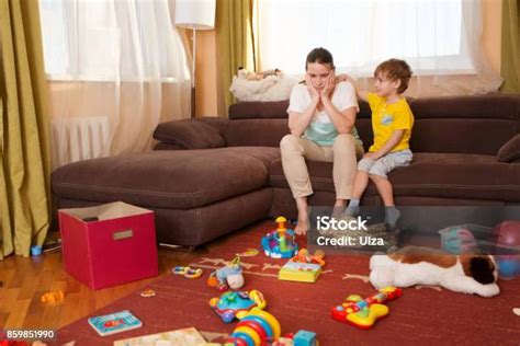 젊은 임신 어머니 고 집에서 그녀의 작은 아들 엄마와 작은 아들 소파에 앉아입니다 엄마 집 정리를 피곤 어린이 장난감에 흩어져 집안에 엉망 완구류에 대한 스톡 사진 및 기타