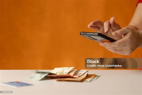 여자의 손이 스마트폰에 타이핑을 하고 있다 250유로 지폐와 신용카드가 테이블 위에 놓여 있다 주황색 배경 지폐 통화에 대한