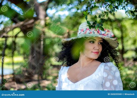 Portrait Of Pretty Young Woman Wearing White Dress And Summer Hat While Posing In The Park Stock