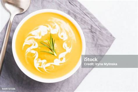 흰색 그릇에 두꺼운 버터넛 스쿼시 비스크를 넣고 흰색 테이블 위에 헤비 크림과 로즈마리로 장식합니다 호박 크림 수프 한 그릇 오버헤드 보기 최소한의 스타일 선택적 초점