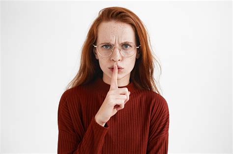쉿 얘기하지 마 짜증 난 화난 젊은 빨간 머리 여교사가 얼굴을 찌푸리고 검지 손가락을 입술에 갖다 대고 쉿 짜증을 내고 역사 수업 중 침묵을 요구하는 스튜디오 샷 귀여운에