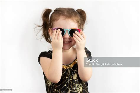 두 개의 포니 테일과 검은 색과 금색 드레스를 입은 어린 소녀가 선글라스를 손으로 덮습니다 흰색 배경에 아이의 스튜디오 사진 2 3 살에 대한 스톡 사진 및 기타 이미지