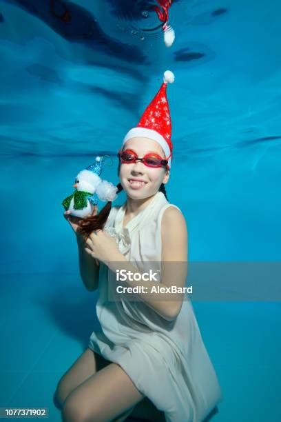그녀의 손에 빨간 산타 모자와 안경 수영 미소와 수영장의 바닥에 앉아 파란 배경에 흰색 드레스에 수 중 포즈 눈사람와 작은 소녀 세로 개념에 대한 스톡 사진 및 기타 이미지