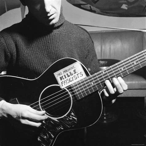 Folk Singer Woody Guthrie Playing Guitar With Sign On It Reading This