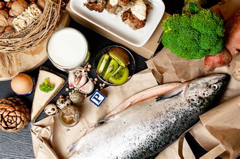 인 연어 생선 잣 땅콩 멸 치 치즈 우유 달걀 브로콜리 키 위 감자를 포함 하는 제품 고기 콩 마늘 라운드 커팅 보드에 검은 나무 배경 0명에 대한 스톡 사진 및 기타