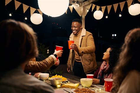 흑인 남성 서 야외 파티에서 축하 다양한 친구의 그룹과 환호 트렌디한 청년 성인 루프탑 데크에 대한 스톡 사진 및 기타 이미지 루프탑 데크 밤 하루 시간대 앉음