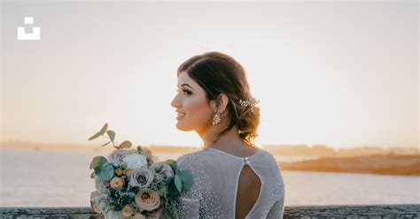 하얀 민소매 드레스를 입은 여자가 일몰 동안 해변에 서 있는 꽃다발을 들고 있다 사진 Unsplash의 무료 시드니 이미지