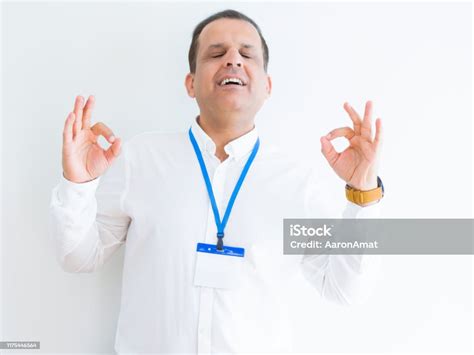 흰색 배경 위에 신분증을 쓰고 있는 중년 사업가가 손가락으로 명상 제스처를 하고 눈을 감고 미소를 짓고 있습니다 요가 개념입니다 개념에 대한 스톡 사진 및 기타 이미지