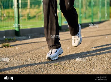 Close Up Of Female Legs In White Sneakers Running Along The Road Near
